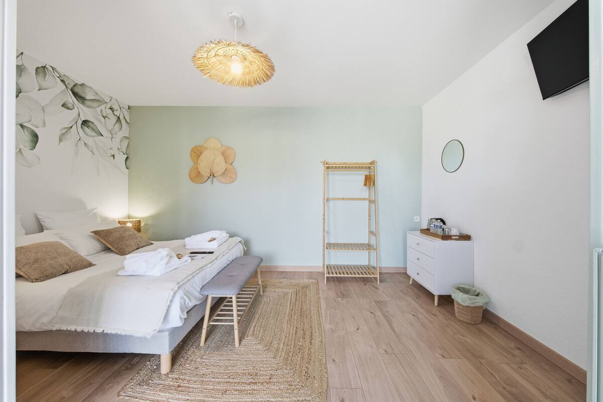 Quarto com cama, mesa de cabeceira, televisão na parede e luminária suspensa.