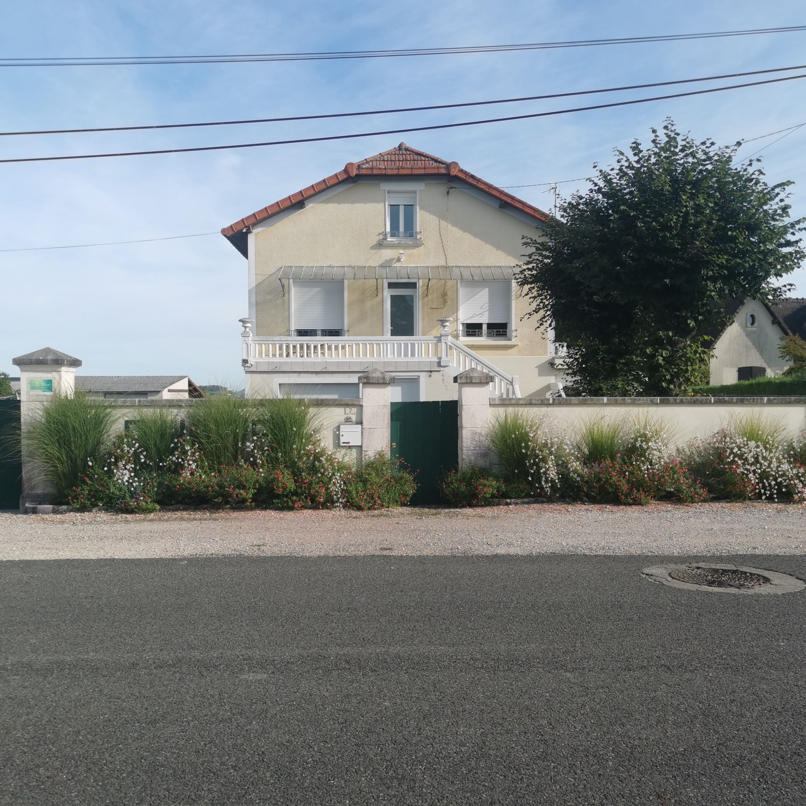 Um edifício de dois andares com varanda, entrada protegida por portão e um pequeno jardim.