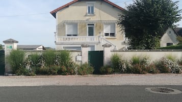 Um edifício de dois andares com varanda, entrada protegida por portão e um pequeno jardim.