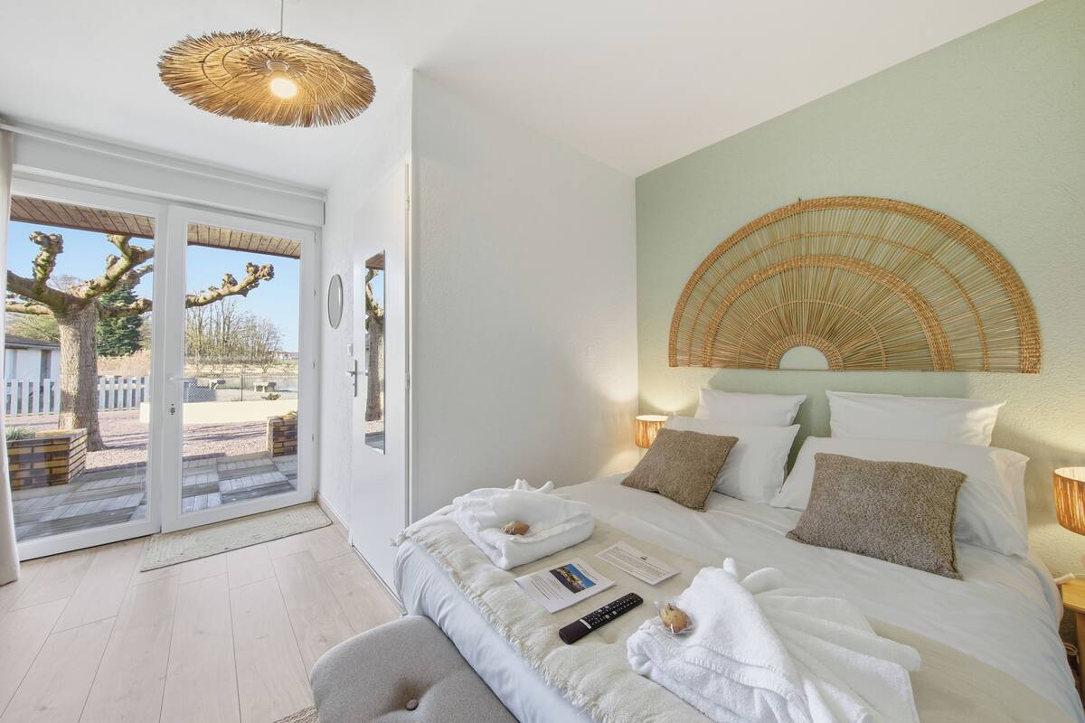 Quarto com cama, almofadas, mesa de cabeceira, abajur, controle remoto e porta que dá para uma varanda.