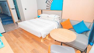 Quarto de hotel moderno com cama, mesa redonda, sofá com almofadas coloridas e decoração de parede xadrez.