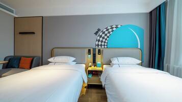 Quarto de hotel com duas camas, uma escrivaninha, uma cadeira, uma mesinha, um espelho e uma janela com cortinas.