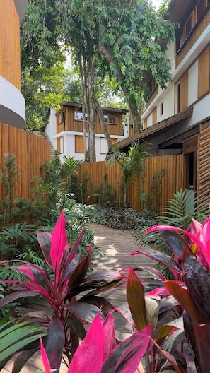 Um pátio com cerca de madeira, um caminho e plantas tropicais.