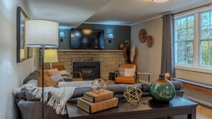 Uma sala de estar com lareira, sofá, poltrona e uma mesa de centro com objetos decorativos.