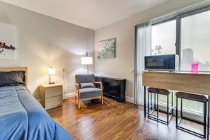 Quarto de hotel moderno com cama, escrivaninha com cadeira, luminária, pintura e vista da cidade pela janela.