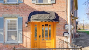 Um edifício de tijolos com uma porta amarela, toldo preto e guarda-corpo de metal na frente.