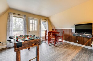 Quarto com mesa de pebolim, televisão e área de refeições com cadeiras e uma mesa.