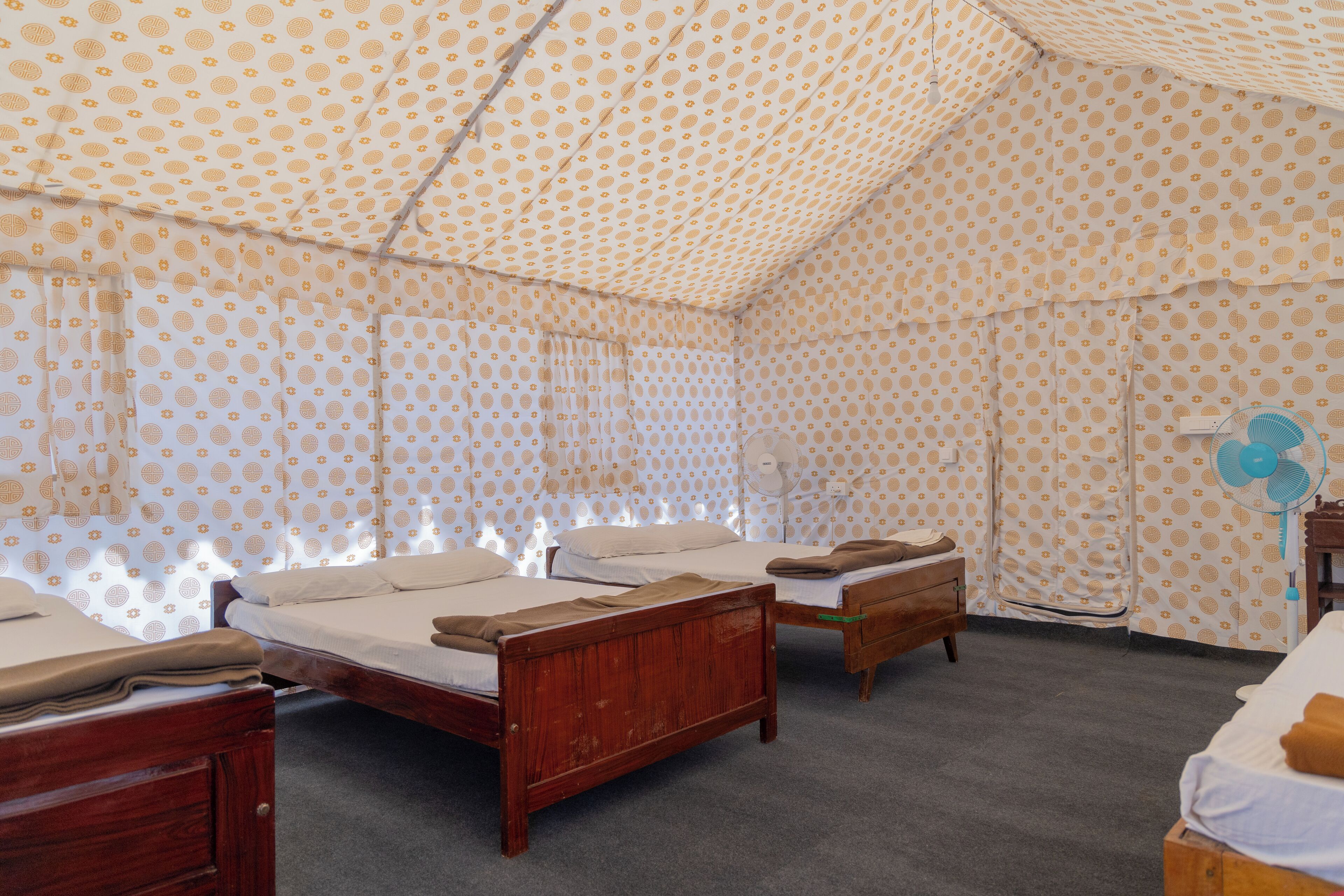 Quarto com duas camas de madeira, um aparador de madeira e um ventilador azul.