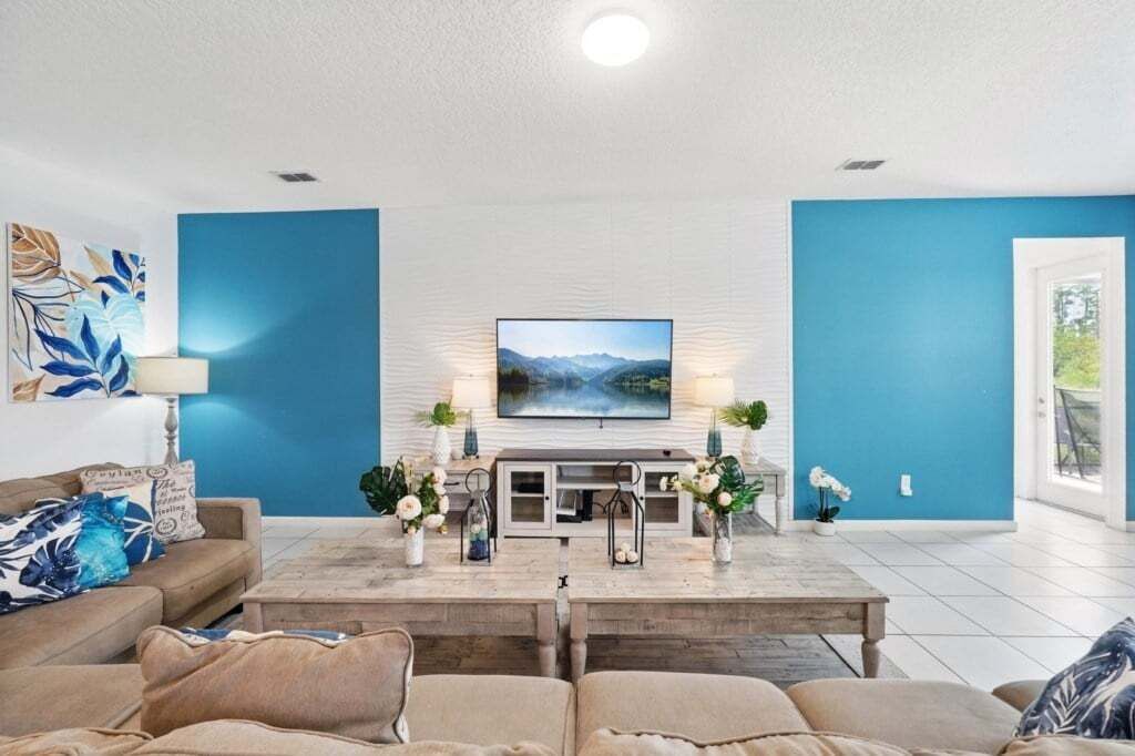 Sala de estar com parede azul de destaque, televisão de tela plana, mesa de centro com objetos decorativos e um sofá.