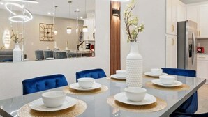 Uma área de jantar moderna com uma mesa comprida posta para seis pessoas, rodeada por cadeiras azuis.