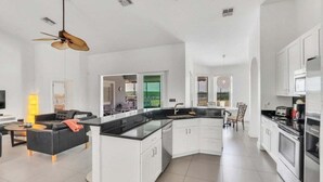 Uma cozinha moderna com armários brancos, uma ilha central e uma área de jantar com um sofá preto e uma mesa de centro.