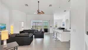 Uma sala ampla com um conjunto de sofás modernos, uma mesa de jantar e uma área de cozinha com balcão.