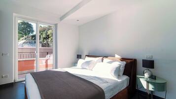 Quarto de hotel com cama, mesa de cabeceira, luminária e porta de vidro deslizante para área externa.