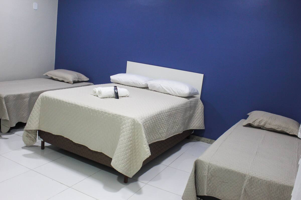 Quarto de hotel com duas camas de solteiro, uma cama grande e uma parede azul decorativa.