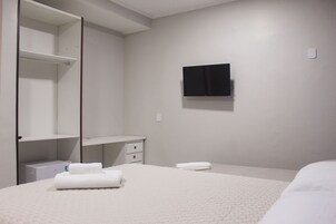 Quarto de hotel com uma cama, televisão na parede, roupeiro e uma pequena mesa de cabeceira.