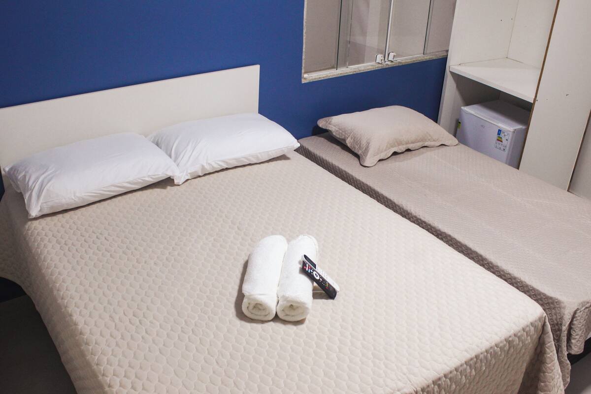 Cama de casal com duas almofadas, um cobertor e duas toalhas enroladas.