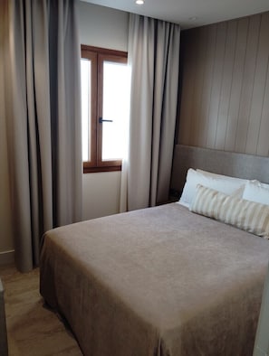 Quarto de hotel com cama, cortinas, janela e cabeceira.