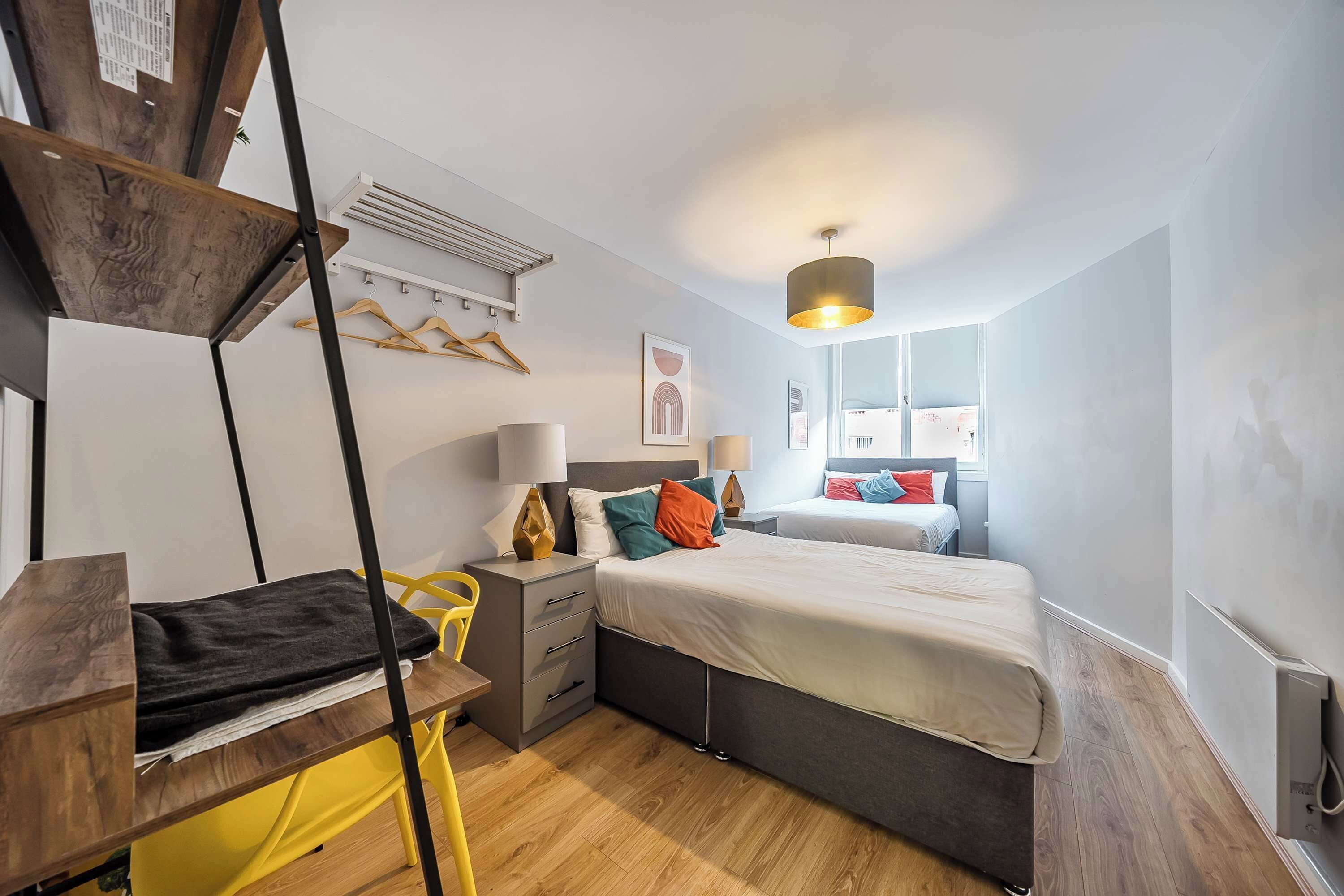 Um quarto moderno com cama, mesas de cabeceira, escrivaninha e luminária suspensa.
