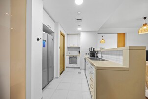 Cozinha moderna com armários brancos, forno embutido, pia de aço inoxidável e porta de madeira.