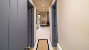 Um corredor com duas portas de cada lado, que dá para um quarto com uma cama e uma cadeira.