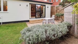 Uma casa moderna com telhado de telhas vermelhas, um pátio com mesa e cadeiras, e um jardim bem cuidado.