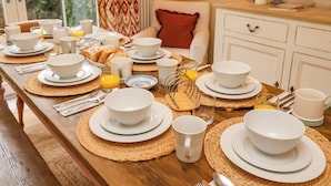 Mesa de café da manhã posta com pratos, tigelas e xícaras brancos, com um sousbento de vime por baixo.