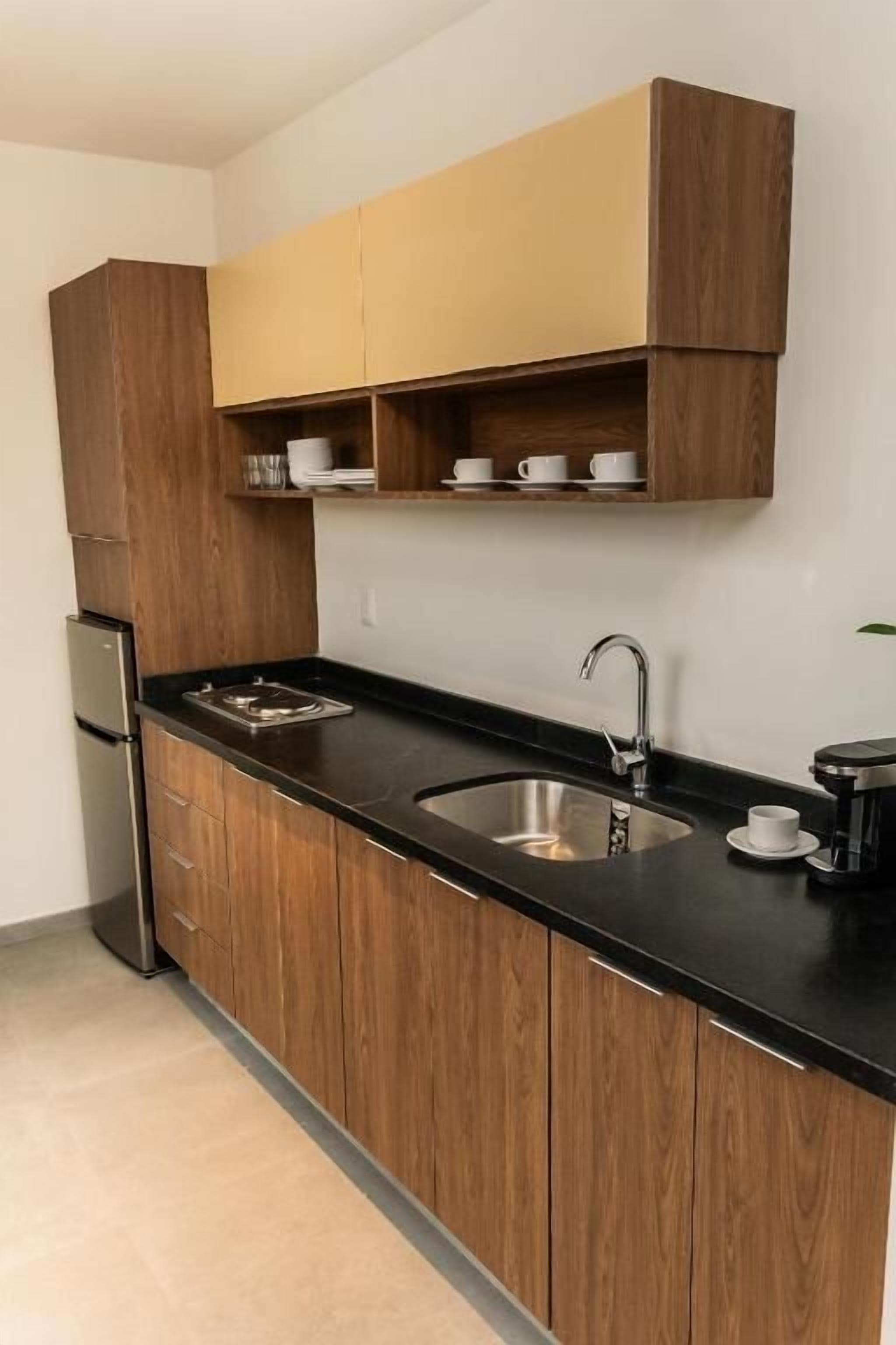 Uma cozinha moderna com armários de madeira, bancada preta, cuba de aço inoxidável e uma cafeteira.