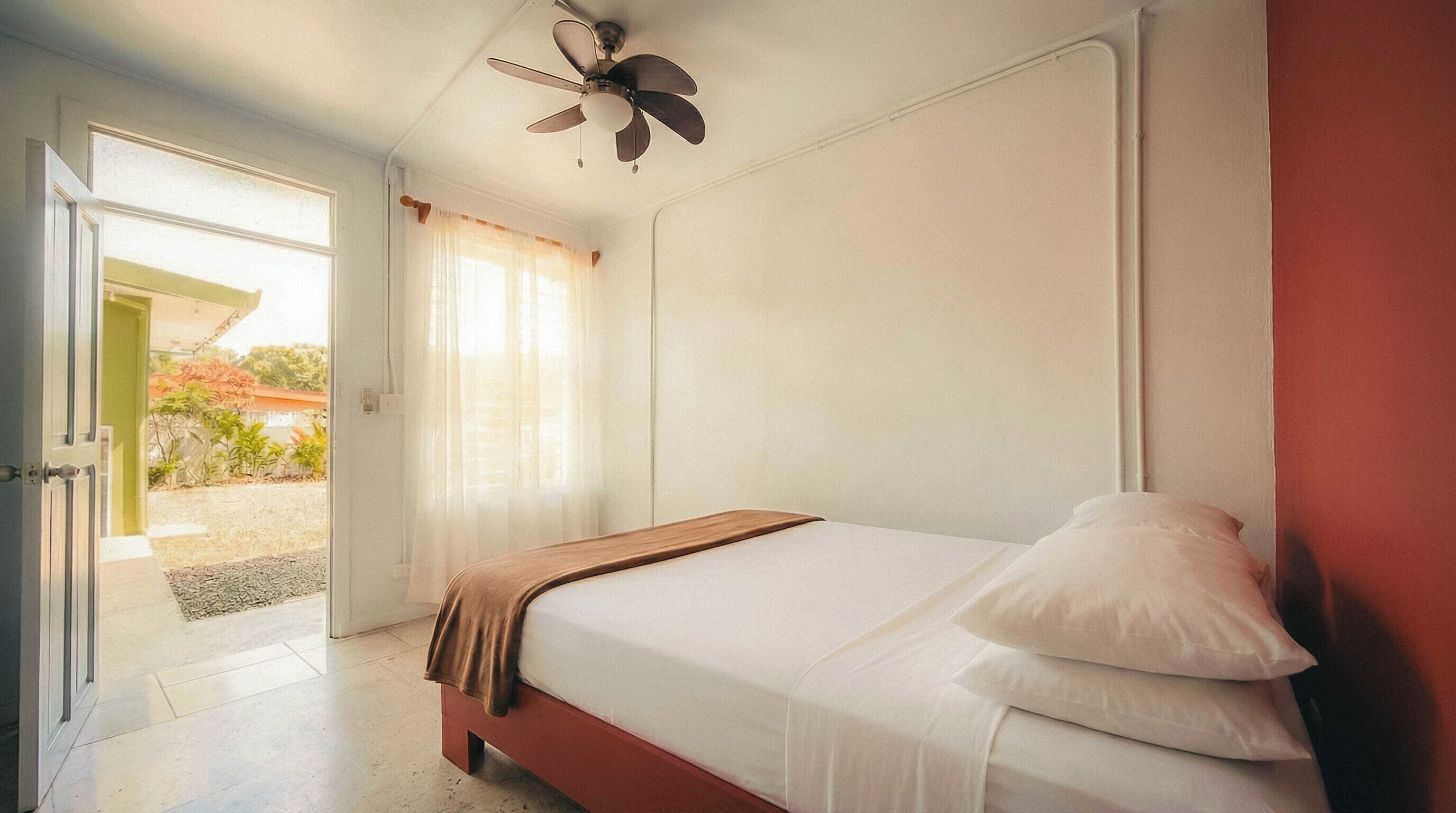 Quarto com cama, ventilador de teto e vista para o exterior.