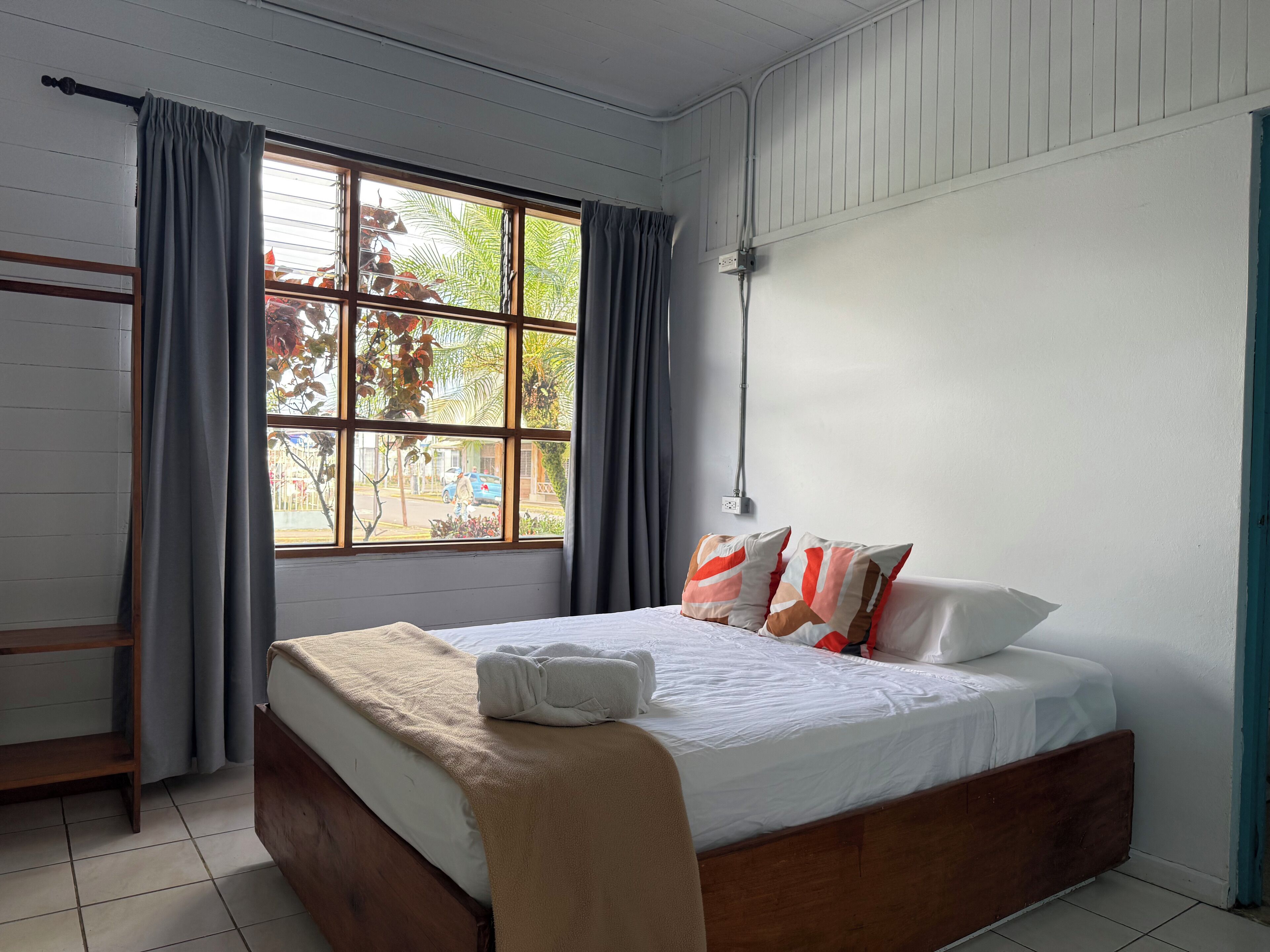 Uma cama bem arrumada com cabeceira de madeira, mesa de cabeceira e uma janela com cortinas.