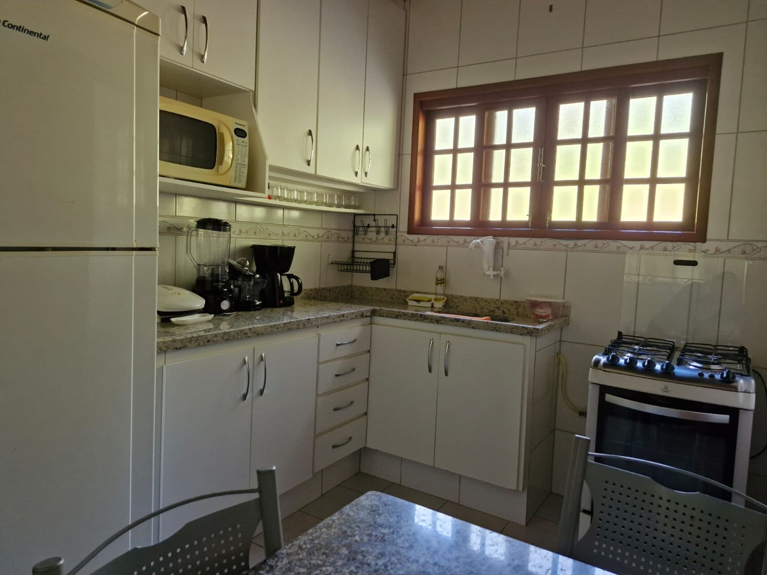 Uma cozinha compacta com armários brancos, micro-ondas, fogão e janela com vidros jateados.