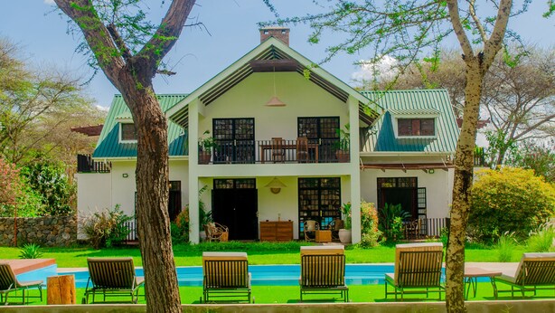 Uma casa de dois andares com piscina, cercada por grama e árvores.