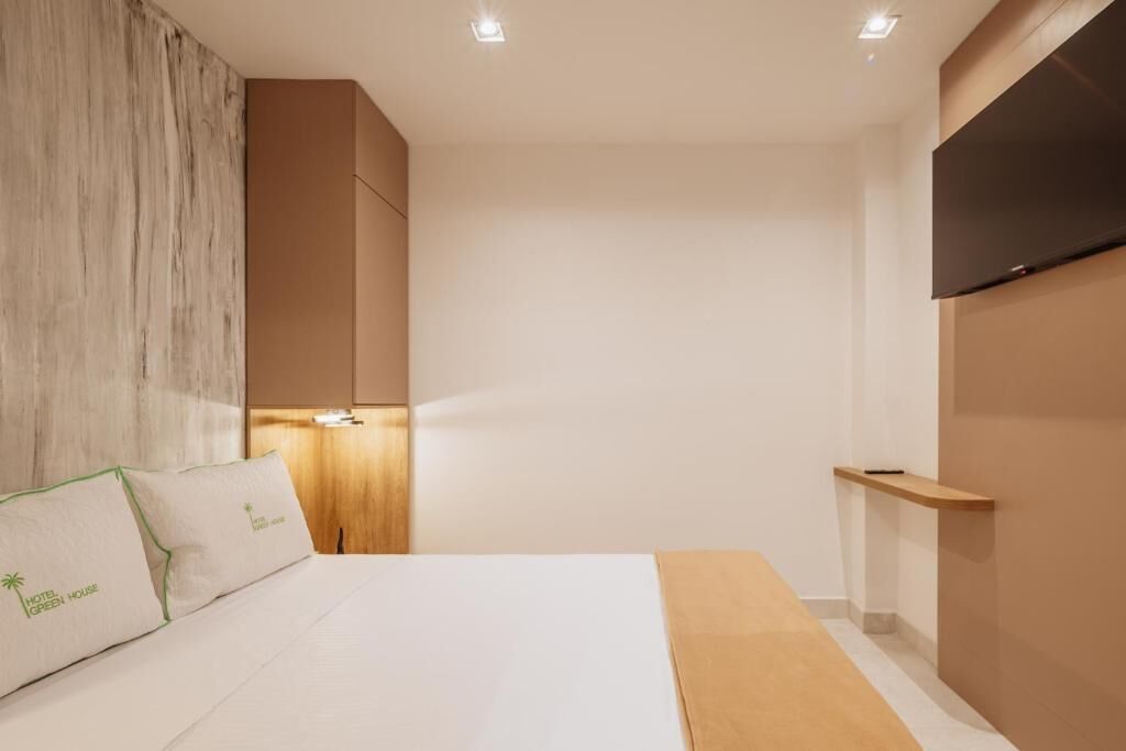 Quarto de hotel moderno com uma cama grande, uma TV montada e um painel de parede em madeira.