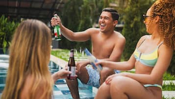 Um grupo de pessoas sentadas à beira de uma piscina, segurando bebidas.