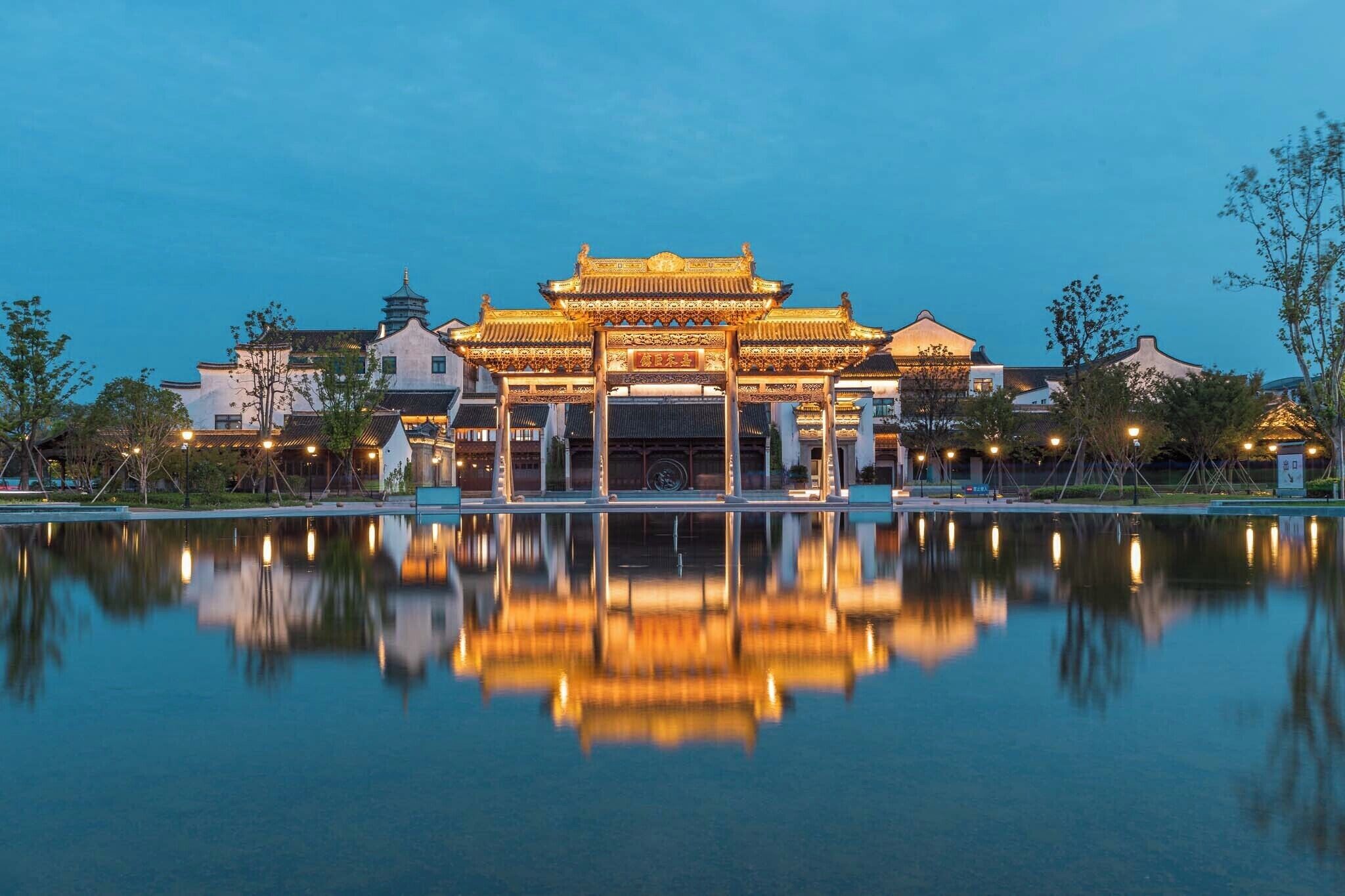 Um portão chinês tradicional refletido na água, rodeado por edifícios modernos e um céu claro.