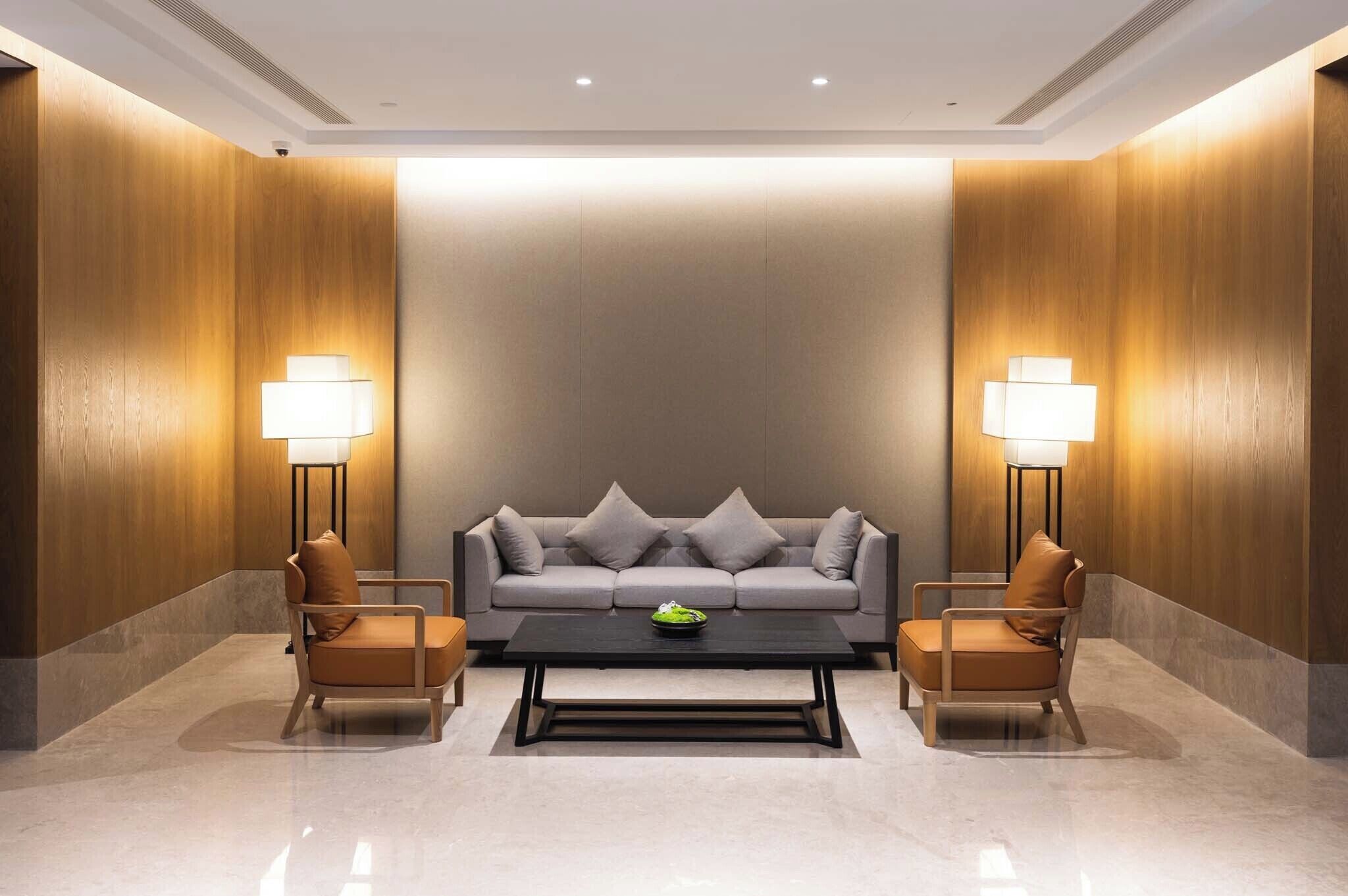 Um hall moderno com um sofá cinzento, duas poltronas, uma mesa de centro preta e duas luminárias de chão.