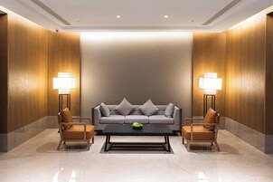 Um hall moderno com um sofá cinzento, duas poltronas, uma mesa de centro preta e duas luminárias de chão.