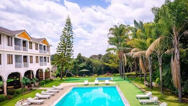 Uma área de piscina com espreguiçadeiras, um edifício com varandas e vegetação tropical.