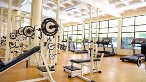 Uma academia com diversos equipamentos de exercícios, janelas amplas e teto alto.