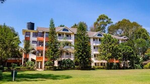 Hotel de vários andares com um pátio central, rodeado por vegetação exuberante e árvores.