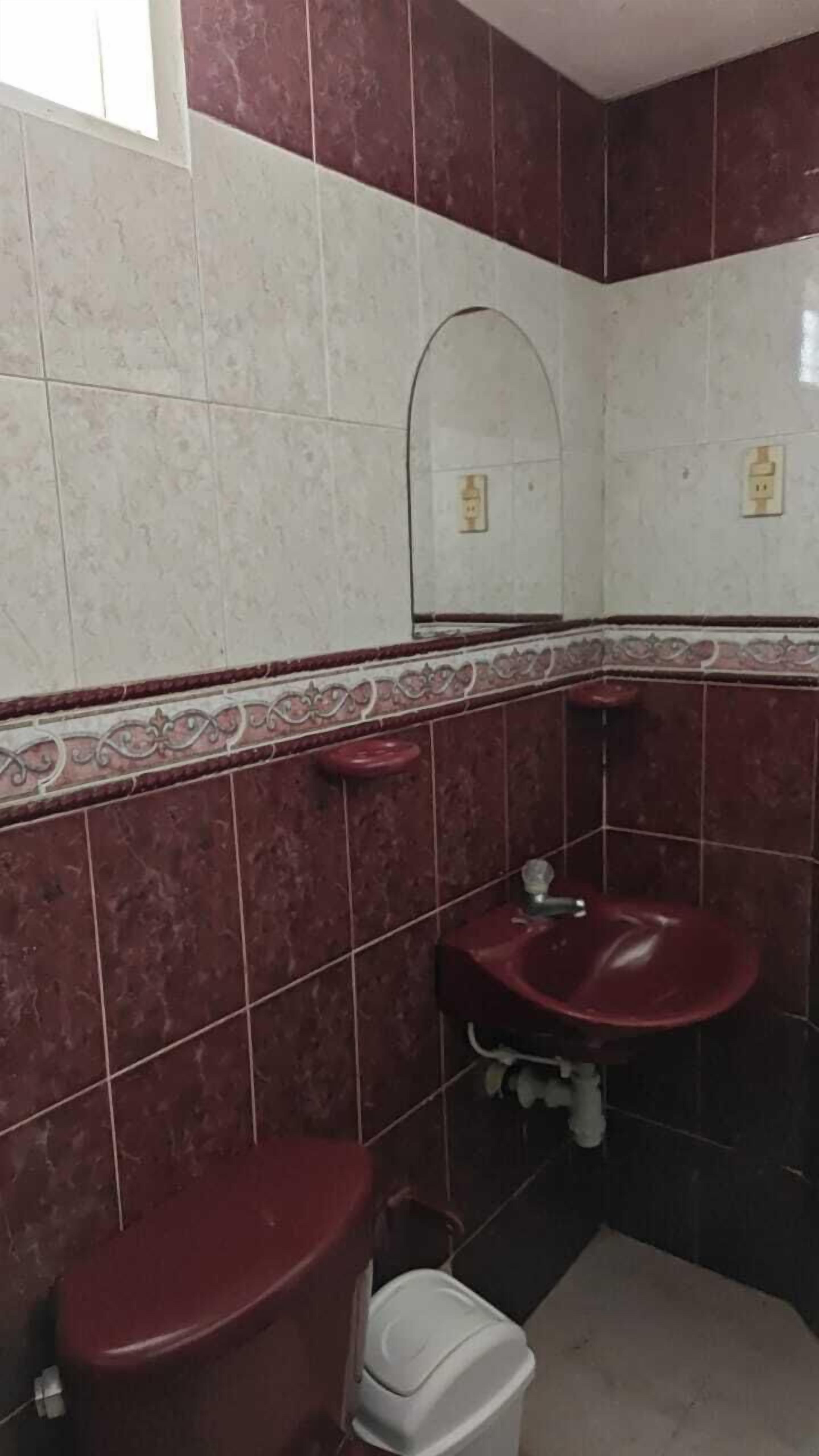 Casa de banho com sanita vermelha, um caixote do lixo branco e lavatório vermelho.