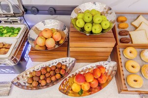 Uma mesa de buffet com diversos alimentos, incluindo frutas, doces e pães.