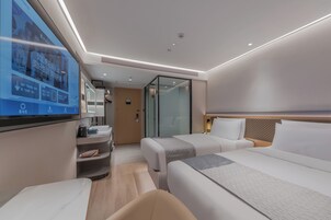Quarto de hotel moderno com uma televisão de tela grande, uma cama, uma mesinha de cabeceira e um guarda-roupa.
