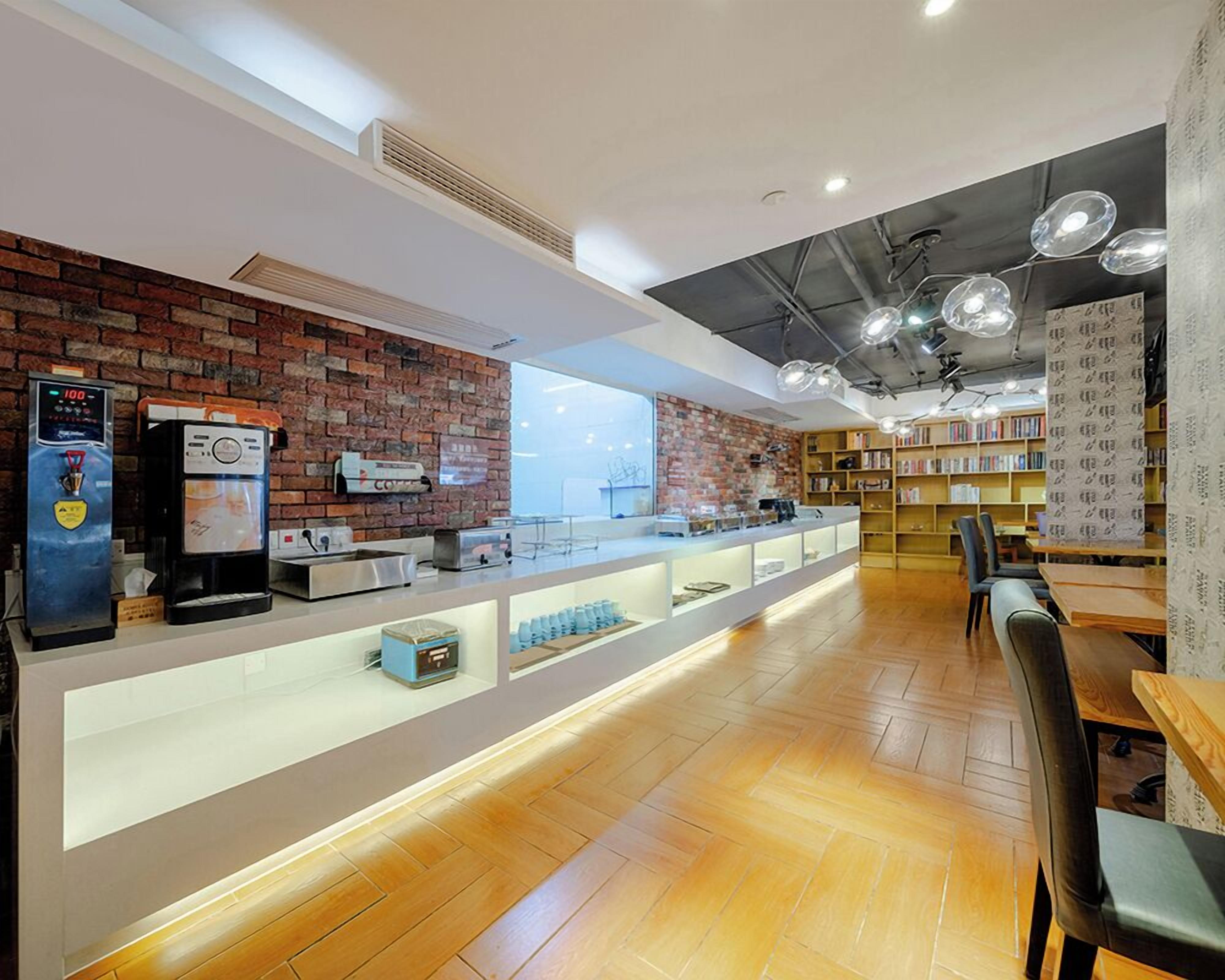 Um café moderno com parede de tijolos, uma máquina de café, um balcão com vitrine de vidro e estantes de livros.