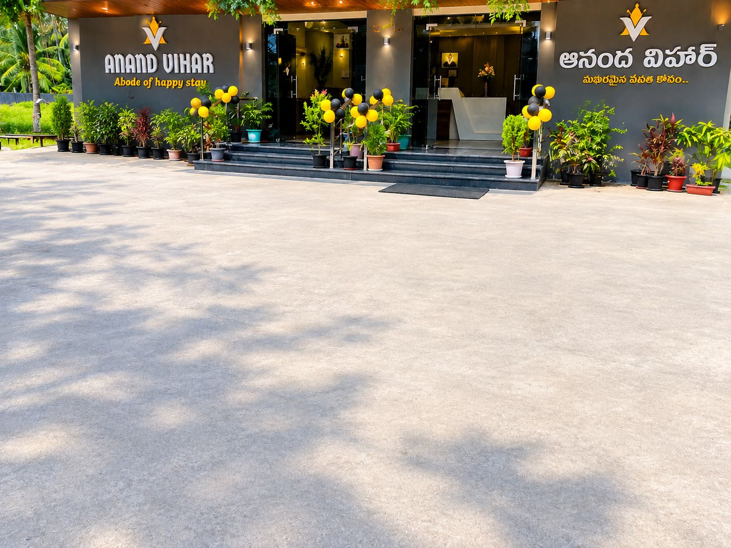 Entrada de hotel com placa, plantas em vasos e caminho bem definido até a entrada.
