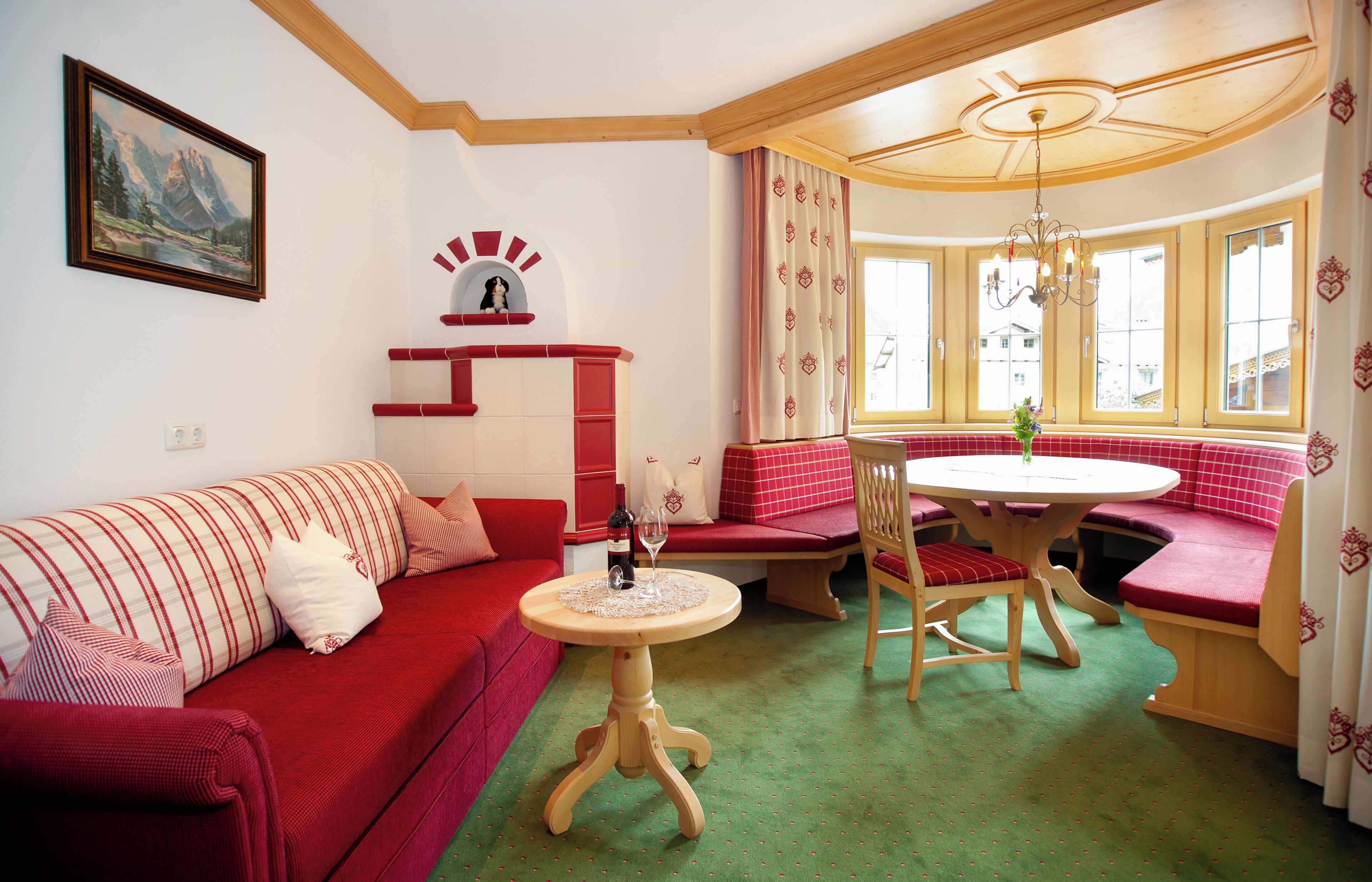 Um quarto aconchegante com um sofá vermelho, uma mesa redonda pequena com uma garrafa e um copo, e um banco com vista para o exterior.