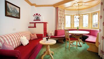 Um quarto aconchegante com um sofá vermelho, uma mesa redonda pequena com uma garrafa e um copo, e um banco com vista para o exterior.