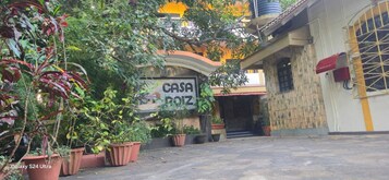 Um edifício com fachada de pedra, plantas em vasos e entrada com portão, identificado com a placa "CASA ROZ".