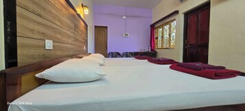 Quarto de hotel com uma cama grande, cabeceira de madeira e parede roxa.