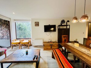 Uma sala de estar moderna com uma grande janela, televisão, mobiliário de madeira e iluminação pendente.