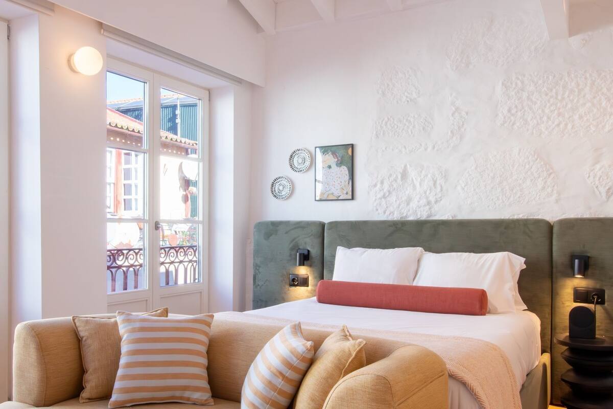 Quarto de hotel com cama, sofá e janela com vista para edifícios.